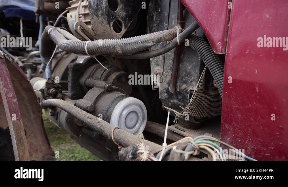 An opened bonnet of a red tractor and its old engine with many wires ...