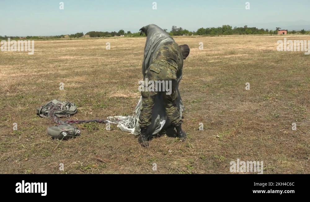 Military parachutist gathering and folding parachute on completing jump ...