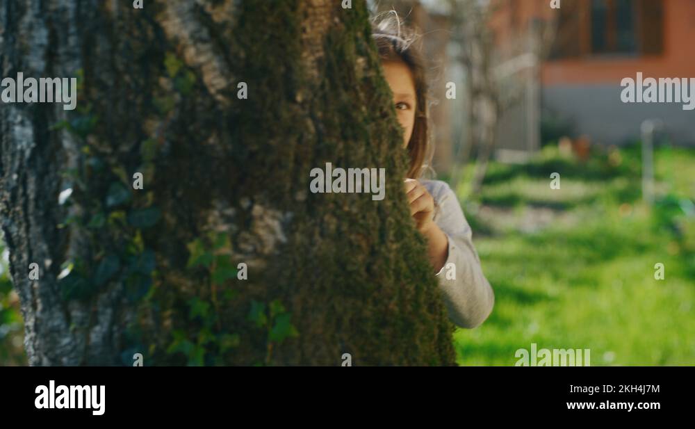 A cute little girl is hiding behind the tree and scary laughing in a ...