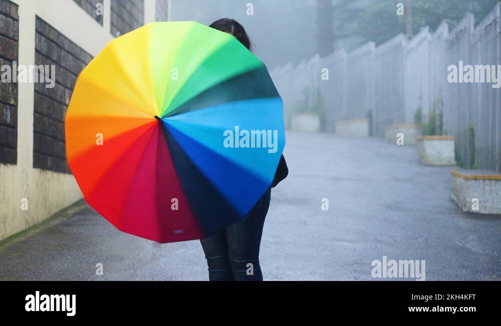 Young indian girl hiding behind a spinning colorful umbrella on a foggy ...