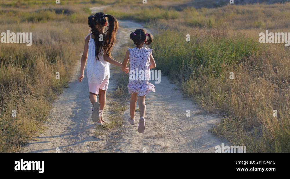 Back view middle plan two beautiful little girls running along a dusty ...