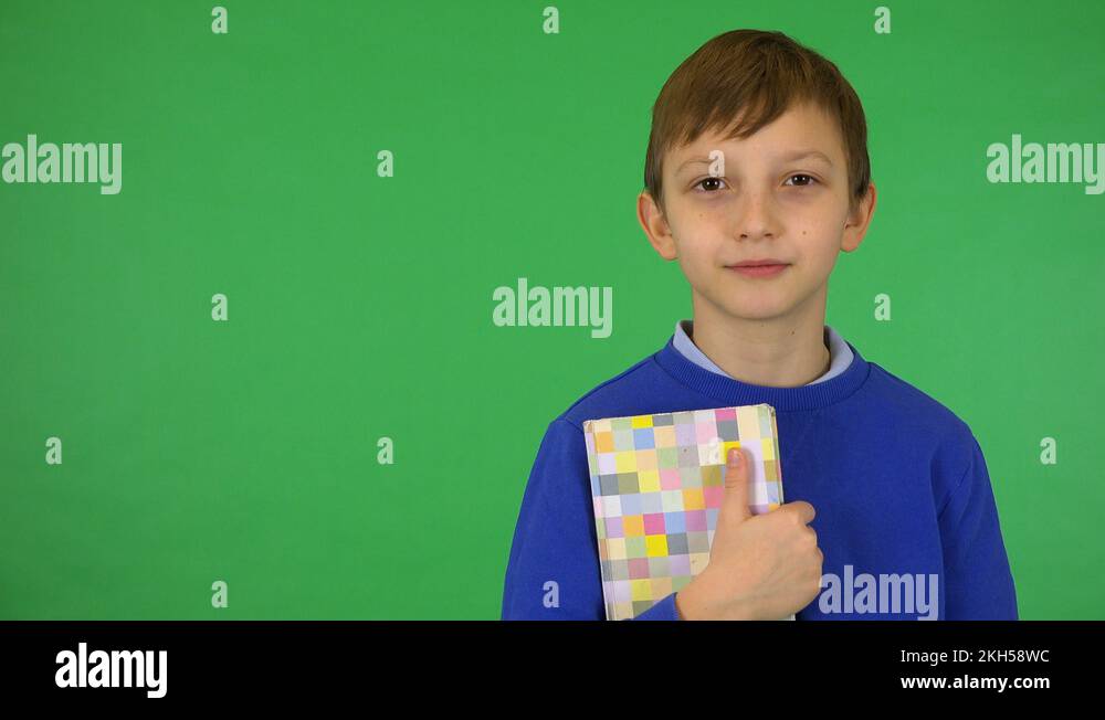 A young cute boy holds a book and smiles at the camera - green screen ...