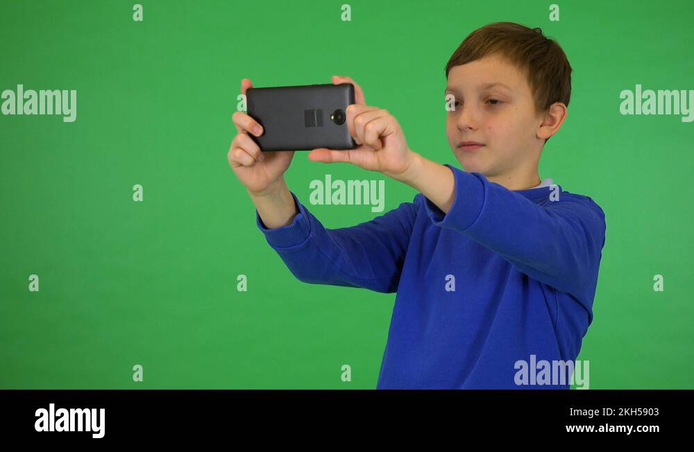 A young cute boy takes pictures with a smartphone - green screen studio ...