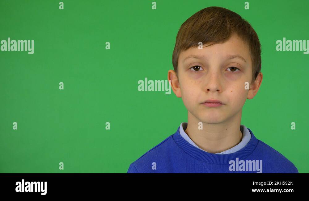 A young cute boy looks seriously at the camera - closeup - green screen ...