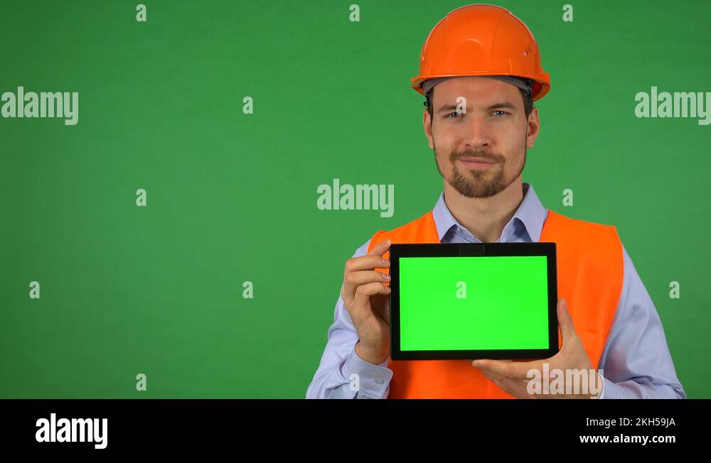 A young handsome construction worker shows a tablet with green screen ...