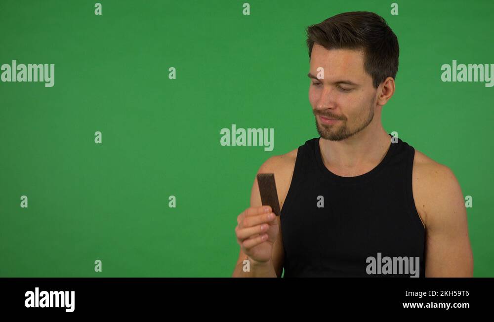 A young handsome athlete eats a protein candy bar - green screen studio ...