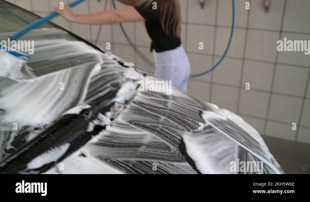 young woman scrubbing her car windshield at a self service car wash ...