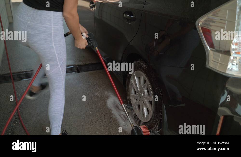 young woman scrubbing her car wheels and tires at a self service car ...