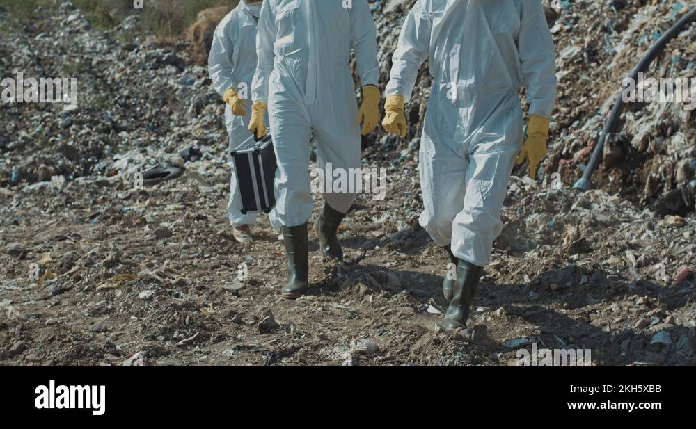 Ecology scientists in white suits walking out of trash waste dump ...