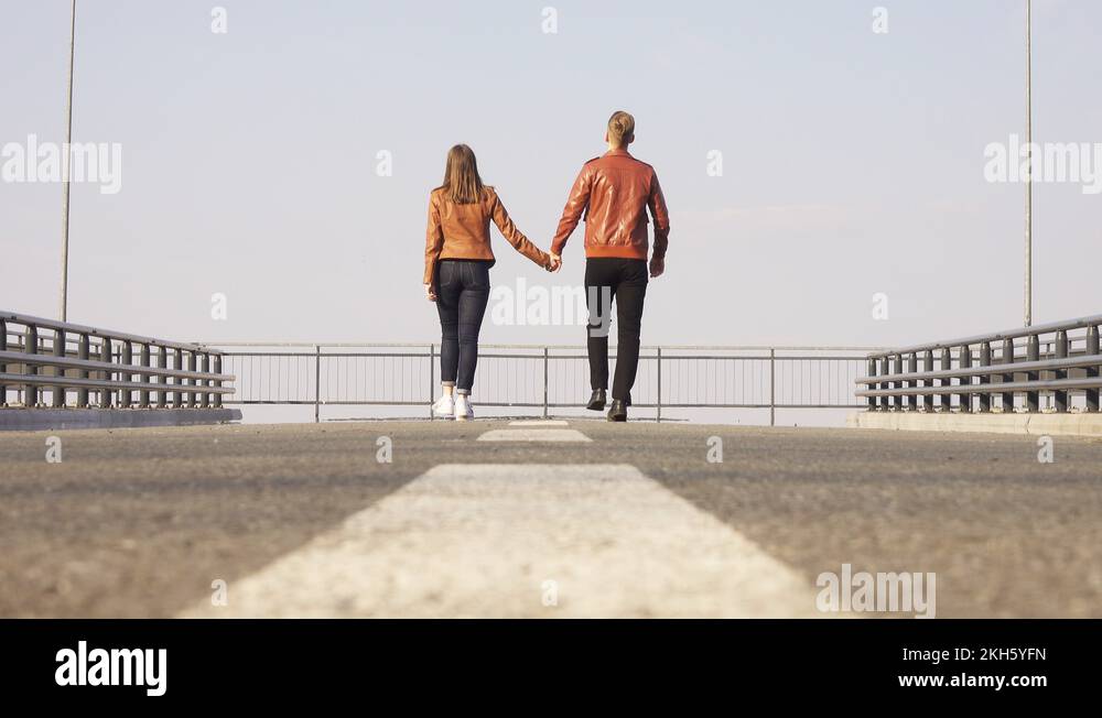 Guy and girl in leather jacket slowly walk away from camera, holding ...