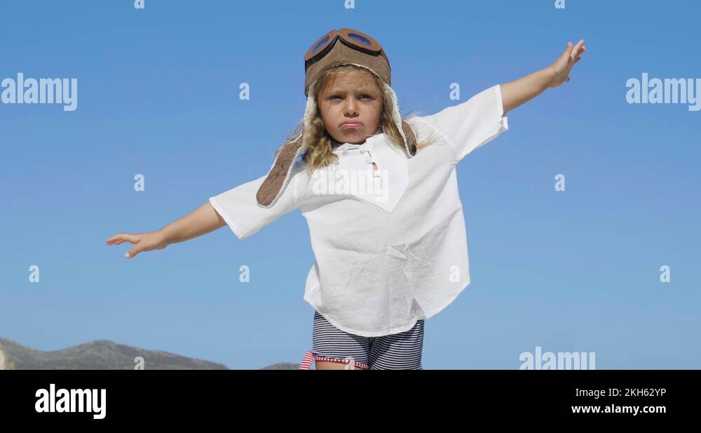 A happy little girl dressed as aviator having fun to fly with her arms ...