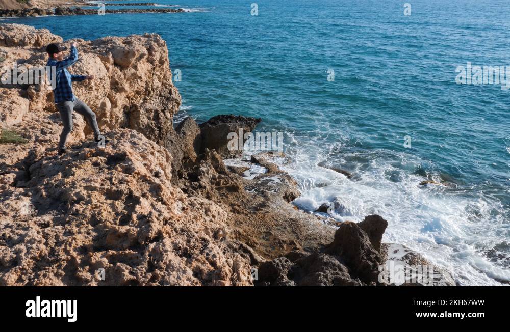 Young guy stands on rocks and throws stones into water. Caucasian boy ...