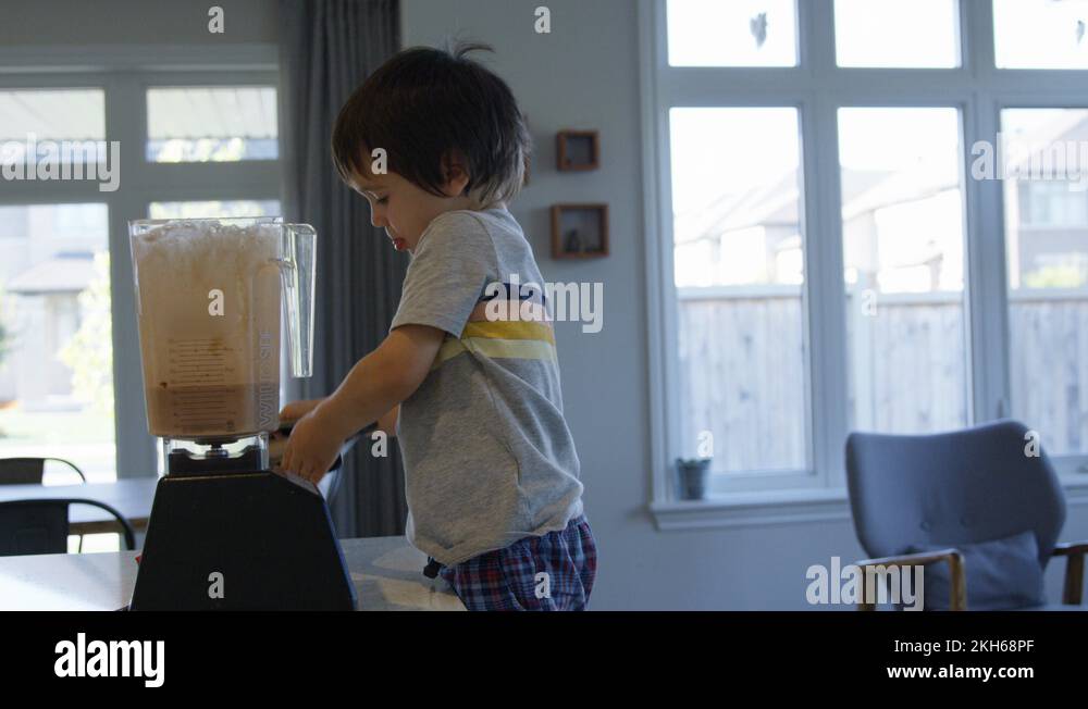 Toddler boy taste tests chocolate smoothie from blender - wide shot ...