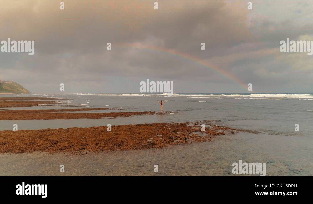 girl in a bathing suit standing in the shallows of the sea, waving his ...