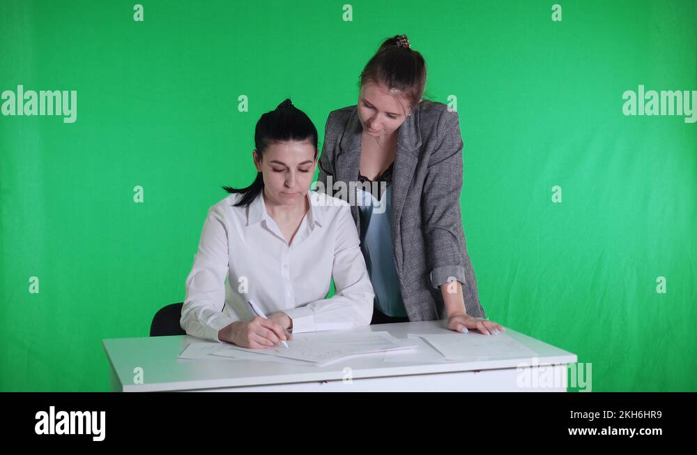 Two successful business women sign contract. Green wall background ...