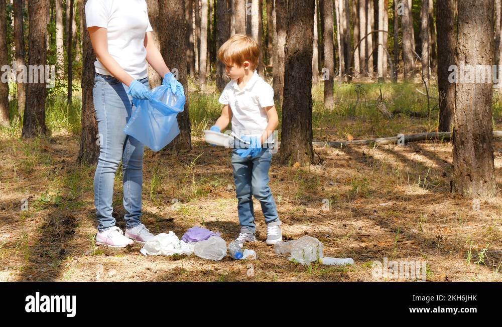 A little boy collects garbage in the woods and puts it in a bag with ...