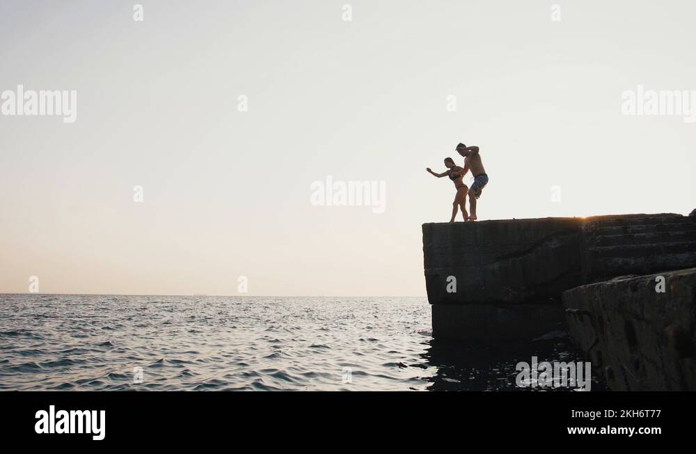 Young woman and man synchronously doing trick jump from a pier into the ...