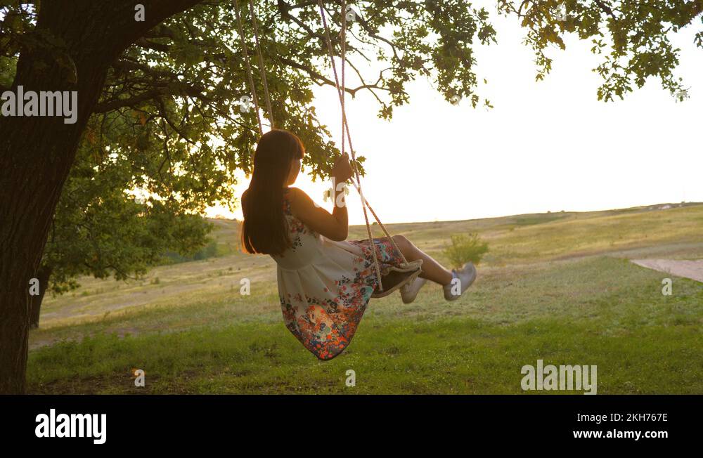 Beautiful girl in a dress in a park on a swing flies. young girl ...