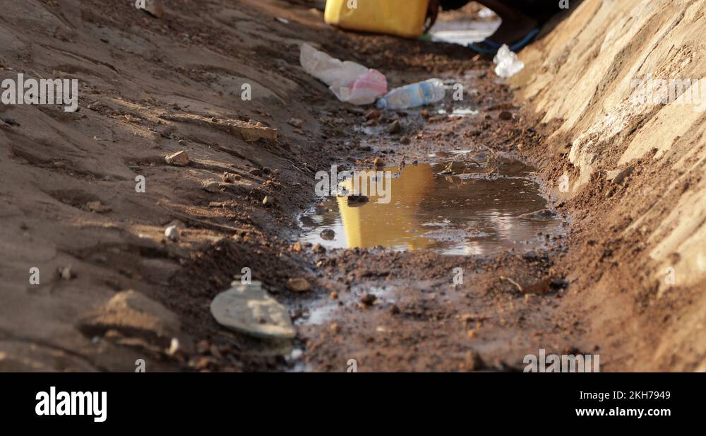 African children using a large bottle to fill water from a dirty water ...