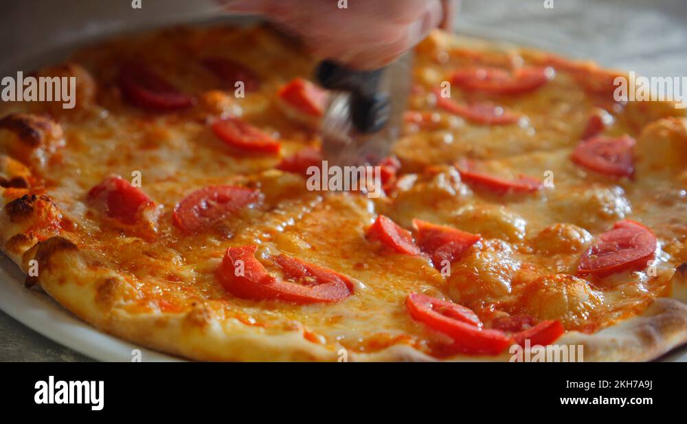 Chef slicing a pepperoni pizza into multiple slices with a pizza cutter ...