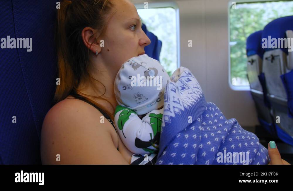 A young mother rides in an electric train and cradles the baby in her ...