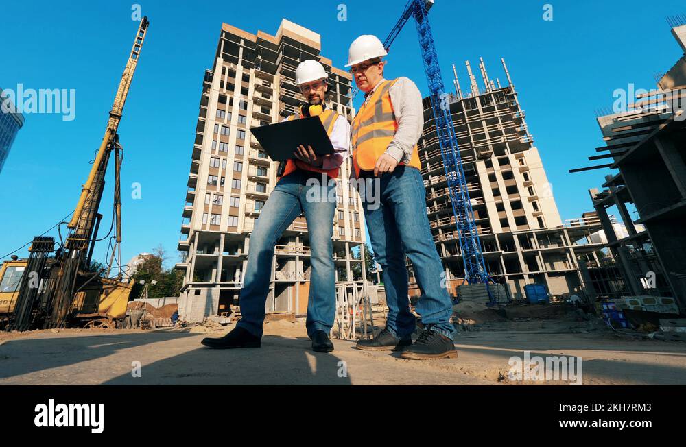 Two engineers are talking next to high-rise buildings in progress ...
