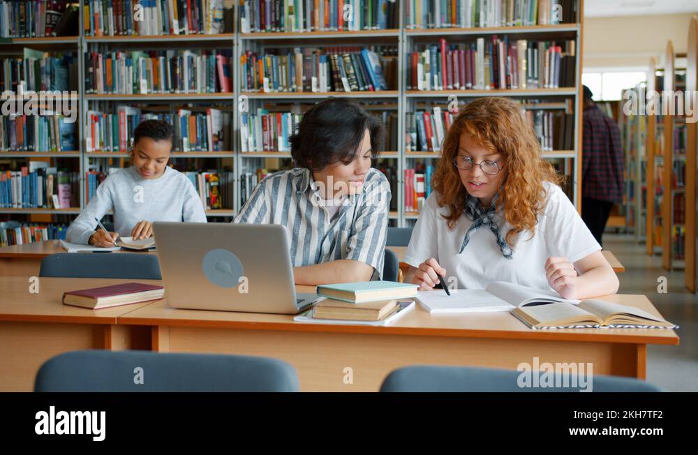 Students studying in library talking using laptop doing research ...