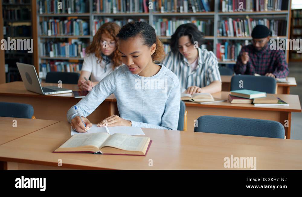 African American girl studying in library reading taking book from male ...