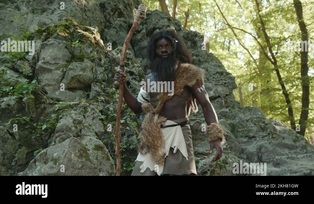 African tarzan tribe leader with animal skin and stick near rocks cave ...