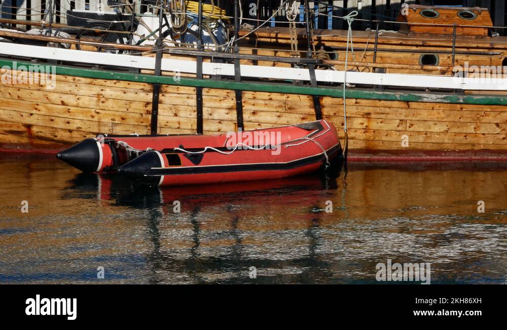 Recreational inflatable red rubber dinghy raft tied to railing of a ...