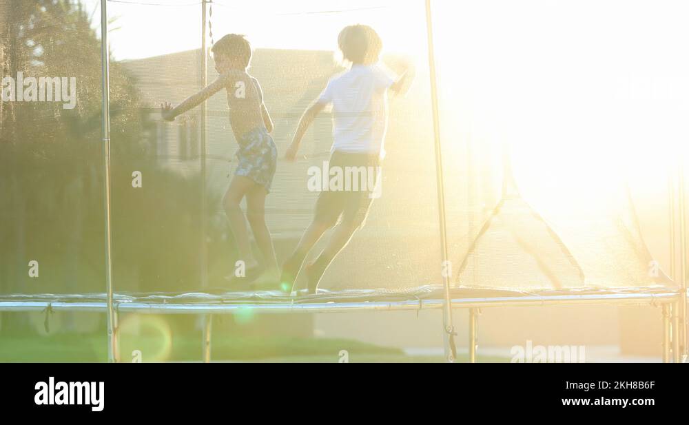 Kids jumping inside trampoline in outdoor setting with lens flare ...
