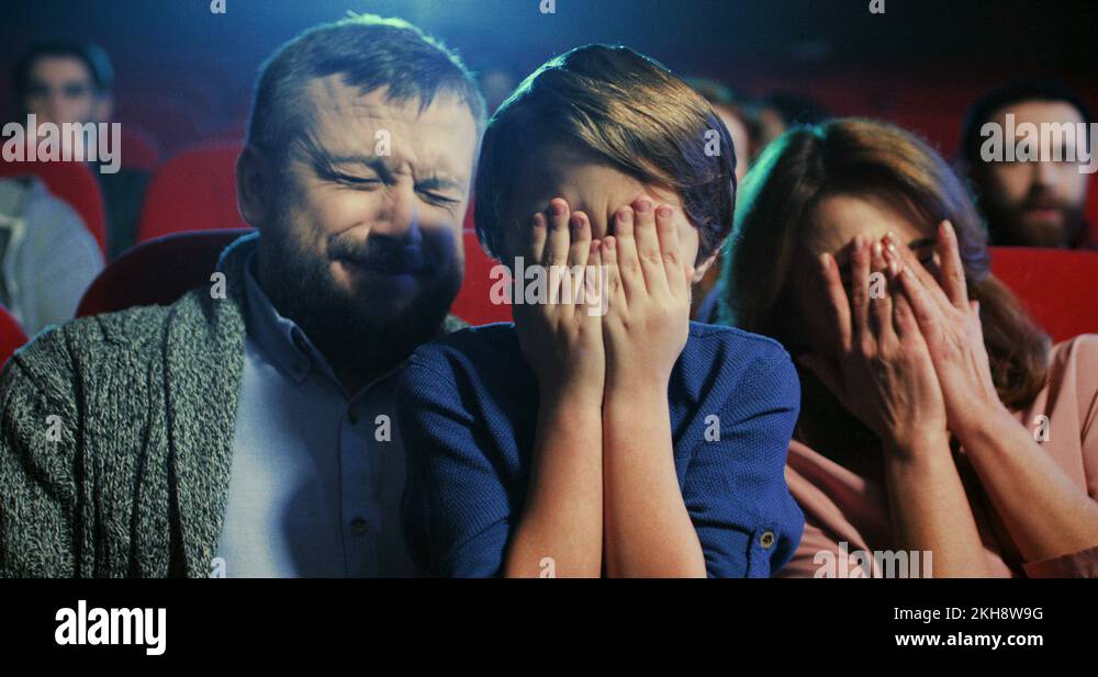 Caucasian mother, father and lttle son sitting in the cinema, closing ...