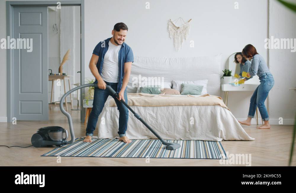 Man and woman having fun during clean-up at home vacuuming and dusting ...
