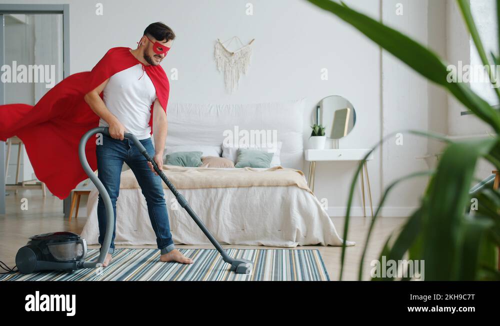 Superman in fluttering cape and mask standing in room with vacuum ...