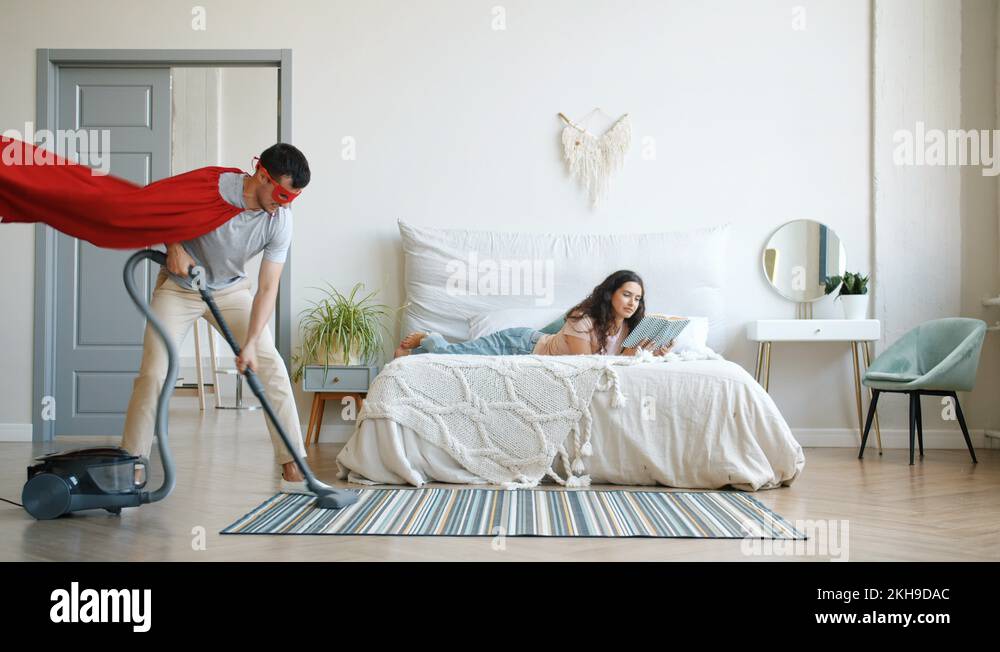 Superman in red cape cleaning floor with vacuum cleaner while girl ...