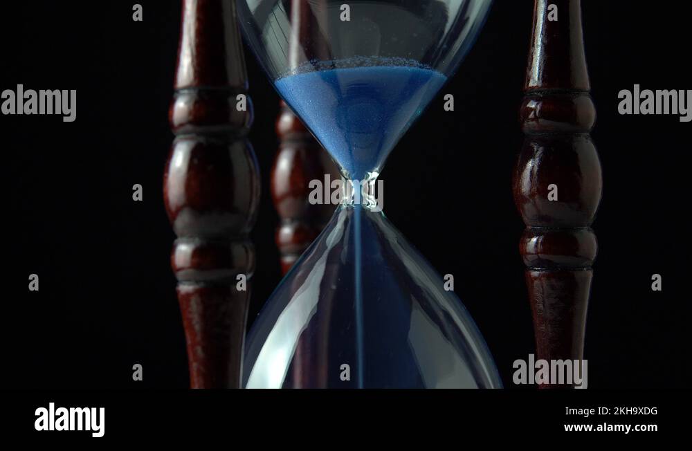 Slow motion rotation of sand timer clock with sand flowing from through ...