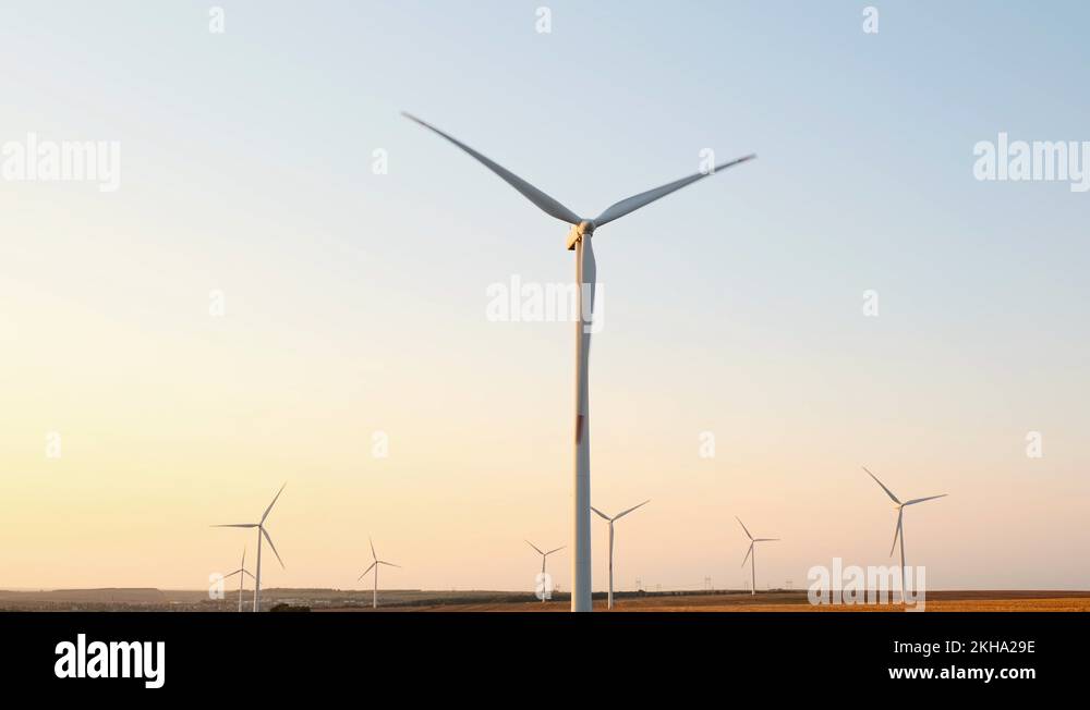 Rotating blades of a large wind turbine in a field orange sunset. Windy ...