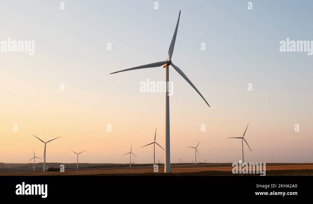Rotating blades of a large wind turbine in a field an orange sunset ...