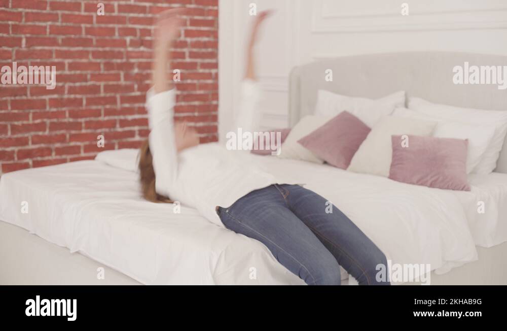 Cute Caucasian girl in white shirt and blue jeans falling on the soft ...