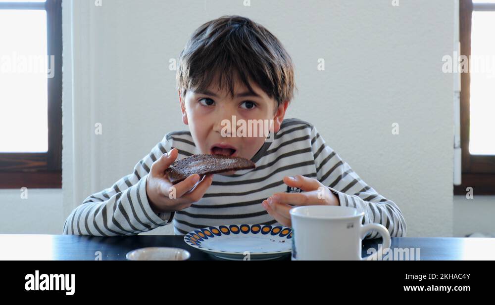 Young boy taking a bite from sliced bread in the morning. Child eating ...