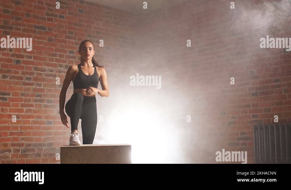 Beautiful female bodybuilder performing squats jumping on fit box in ...