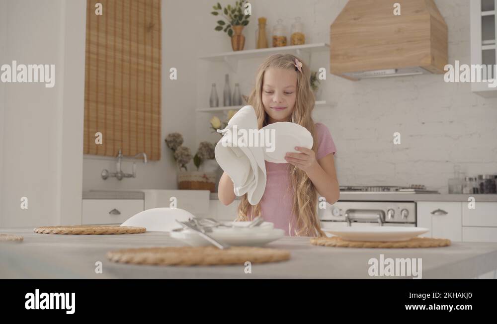 Young bad-tempered Caucasian teenage girl in pink dress wiping plate ...