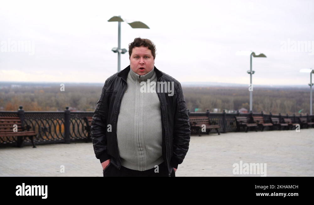 Zoom in portrait of fat man looking at camera and coughing outdoor at ...