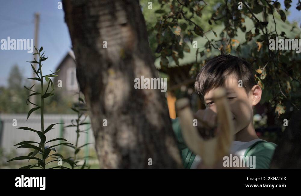 funny boy hides behind a tree and aims with a slingshot outdoors Stock ...