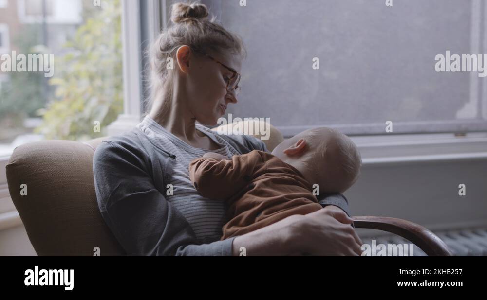 Single Mother comforting baby sitting on chair in living room Stock ...