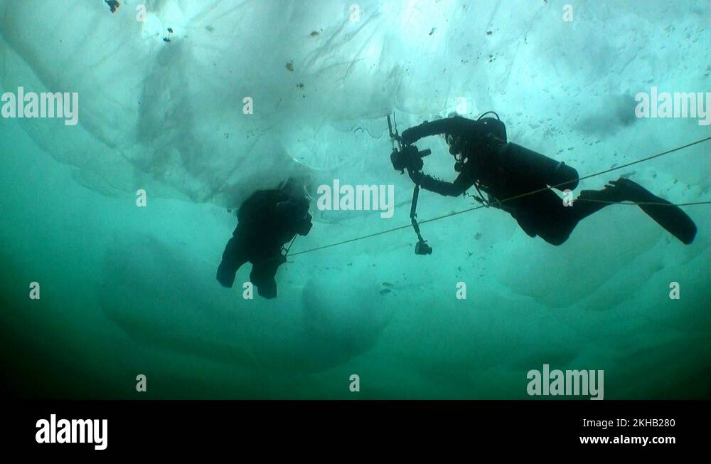 Underwater cameraman with camera and technical diver under ice of lake ...