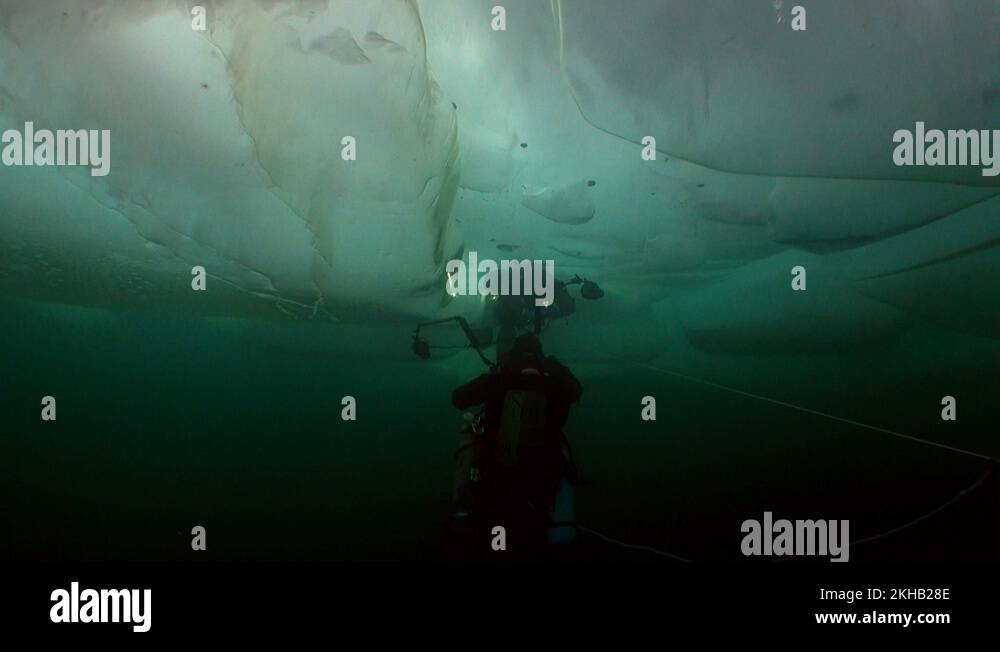 Underwater cameraman with camera and technical diver under ice of lake ...