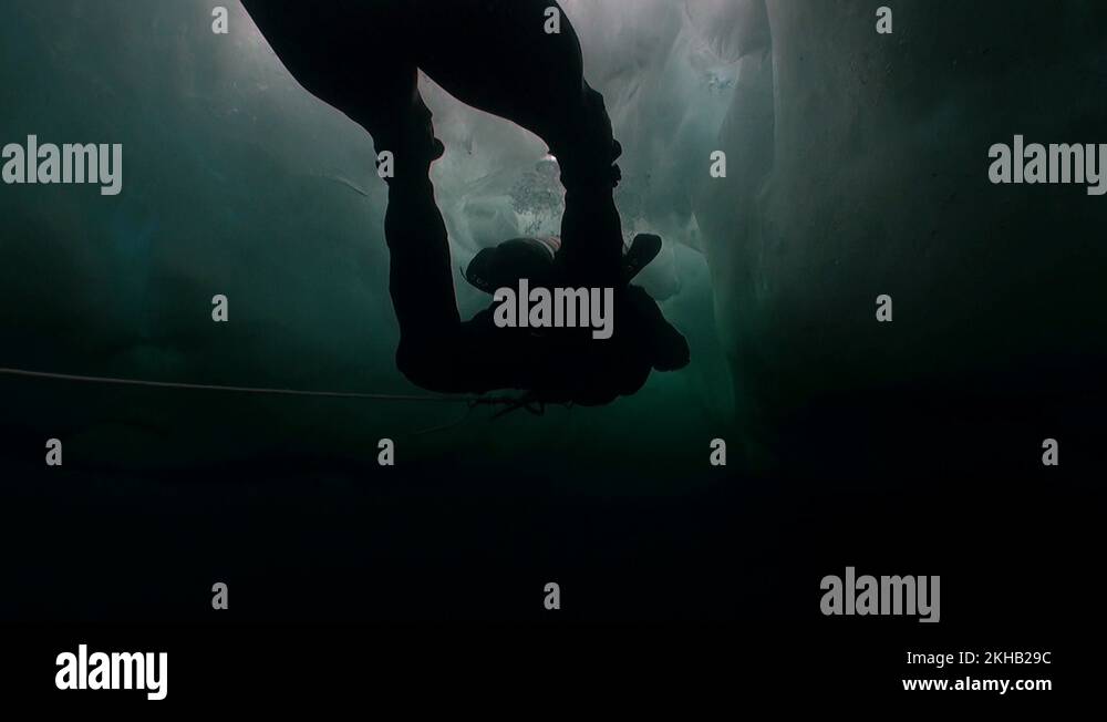 Underwater cameraman with camera and technical diver under ice of lake ...