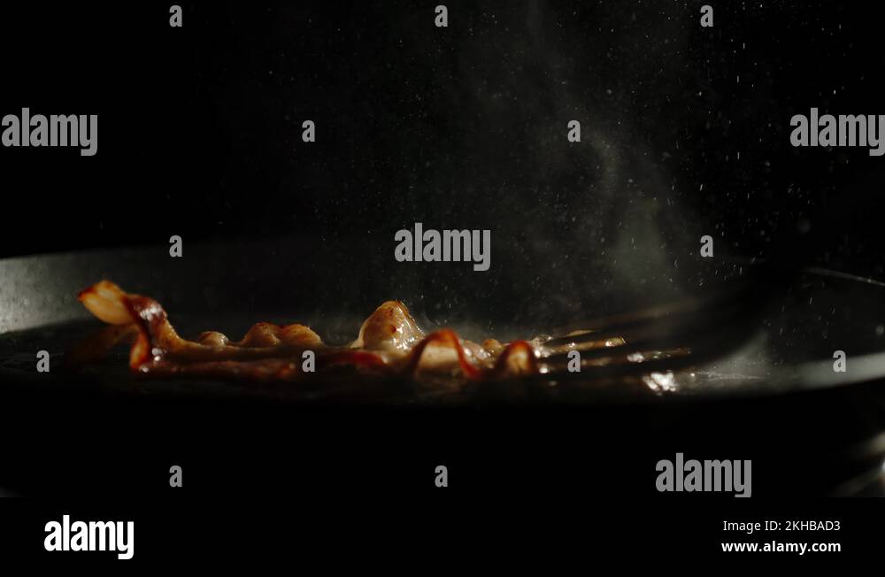 Fork Turning Over A Bacon Slice Frying On A Pan With Splashes Stock ...