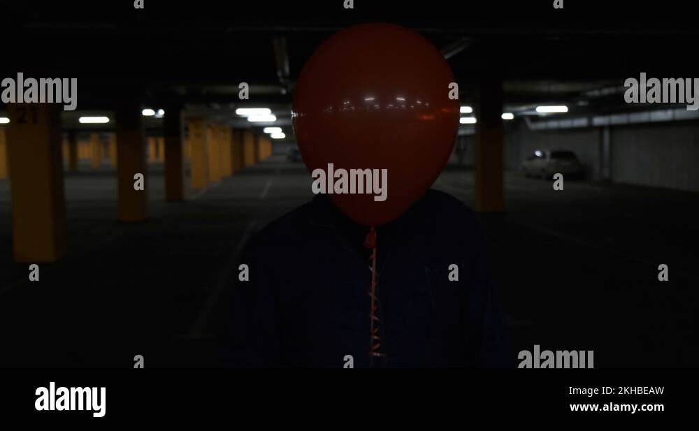 Scary man in creepy leather mask is standing with red ball in dark ...